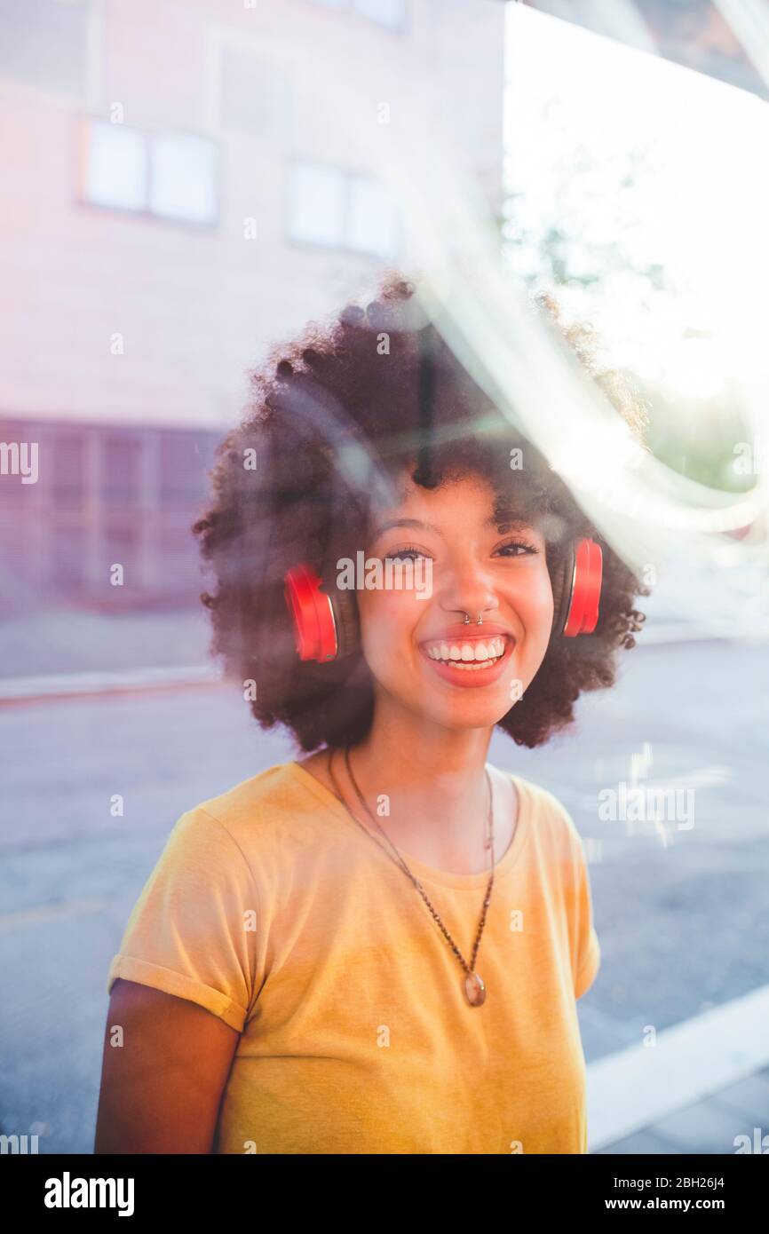 Portrait of happy young woman with afro hairdo listening to music with ...