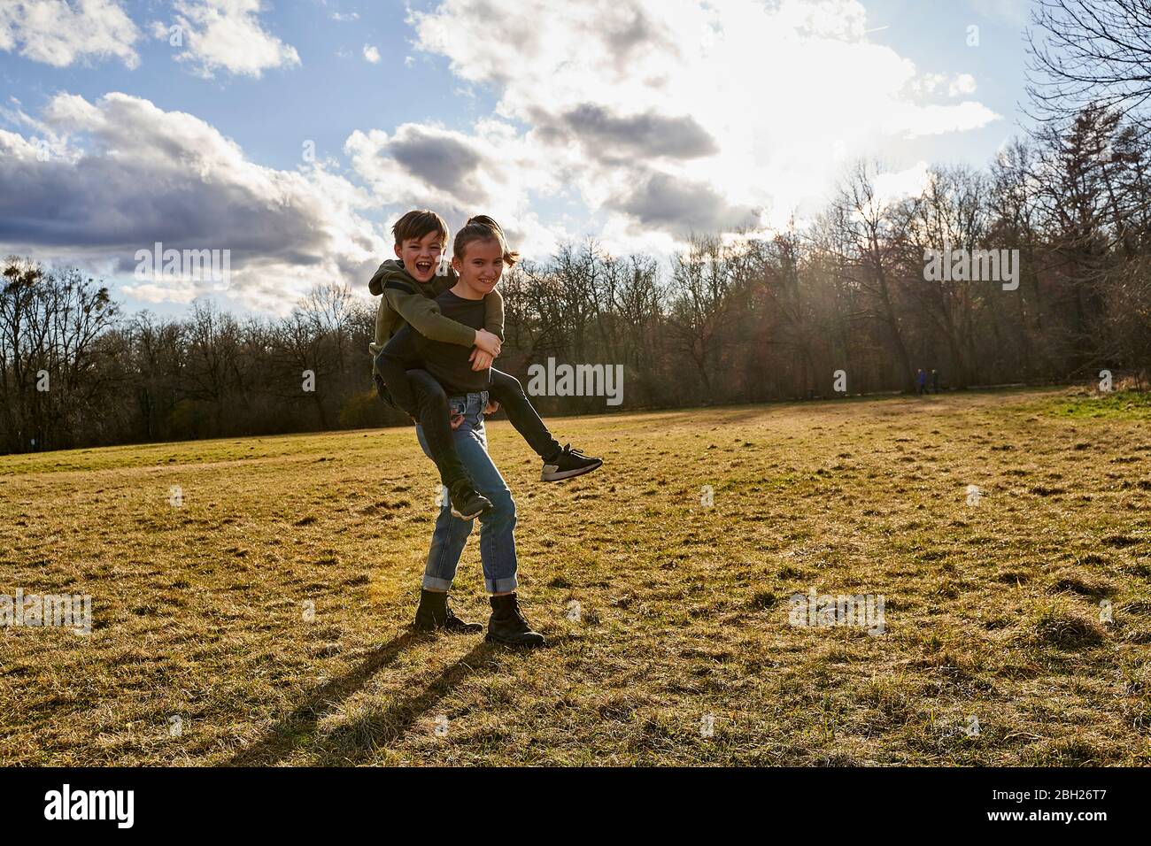 Happy girl carrying brother piggyback on a meadow Stock Photo - Alamy