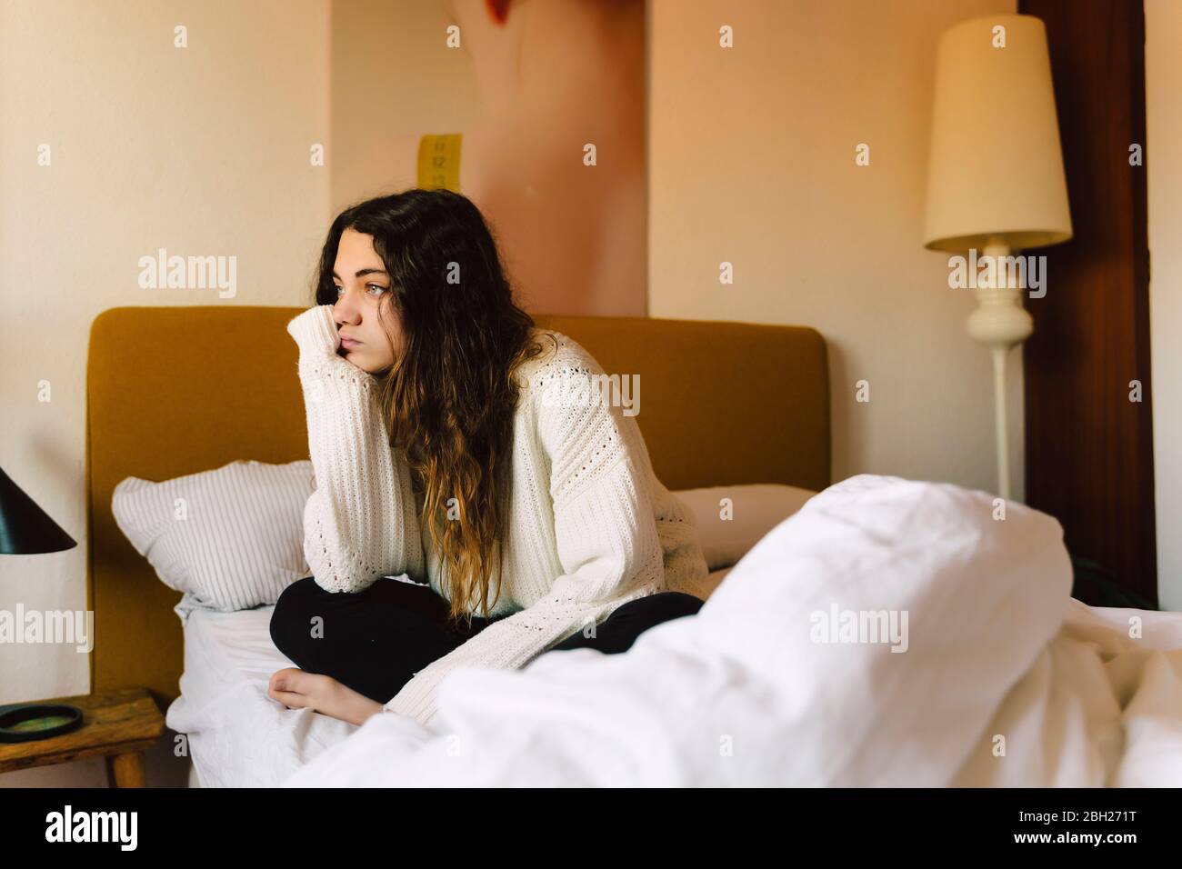 Portrait of sad girl sitting on bed looking at distance Stock Photo - Alamy