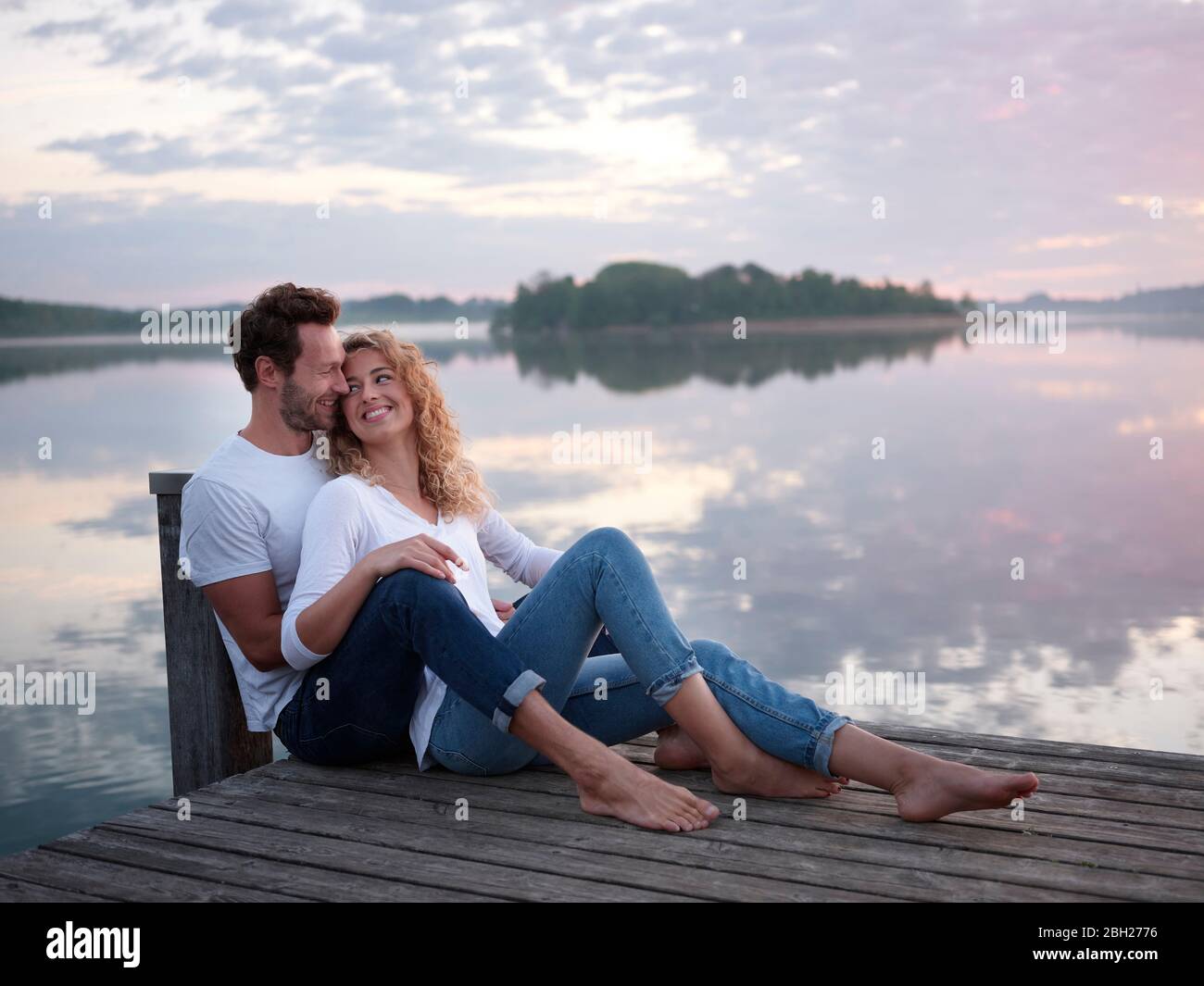 Romantic couple sitting on jetty at the lake Stock Photo - Alamy