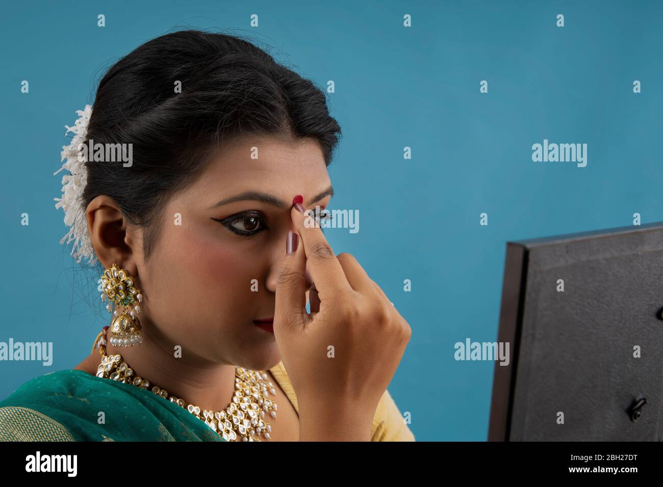 Kathak dancer looking in the mirror putting red bindi on her forehead ...