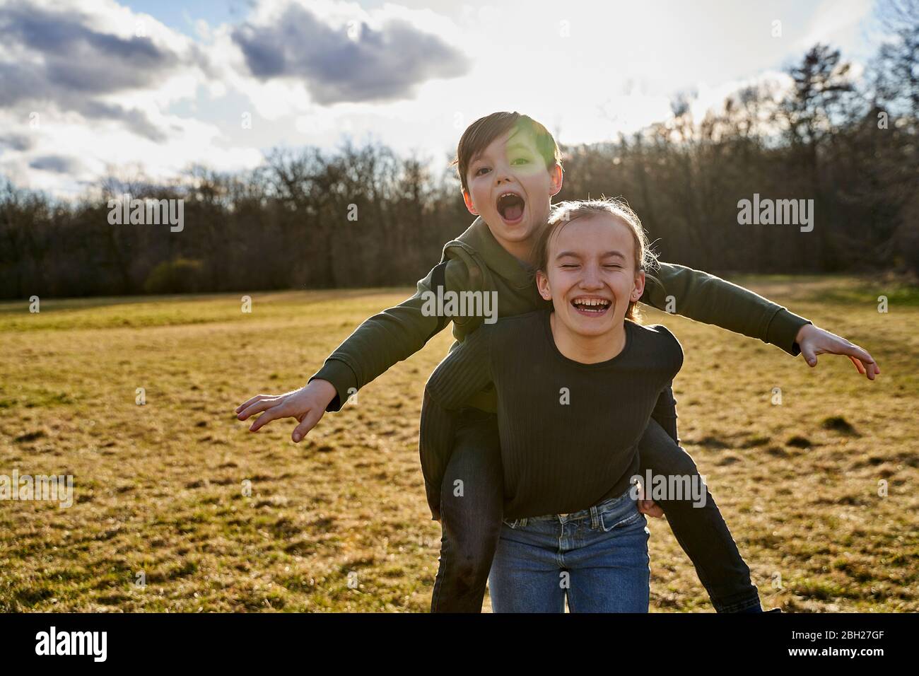 Happy girl carrying brother piggyback on a meadow Stock Photo - Alamy