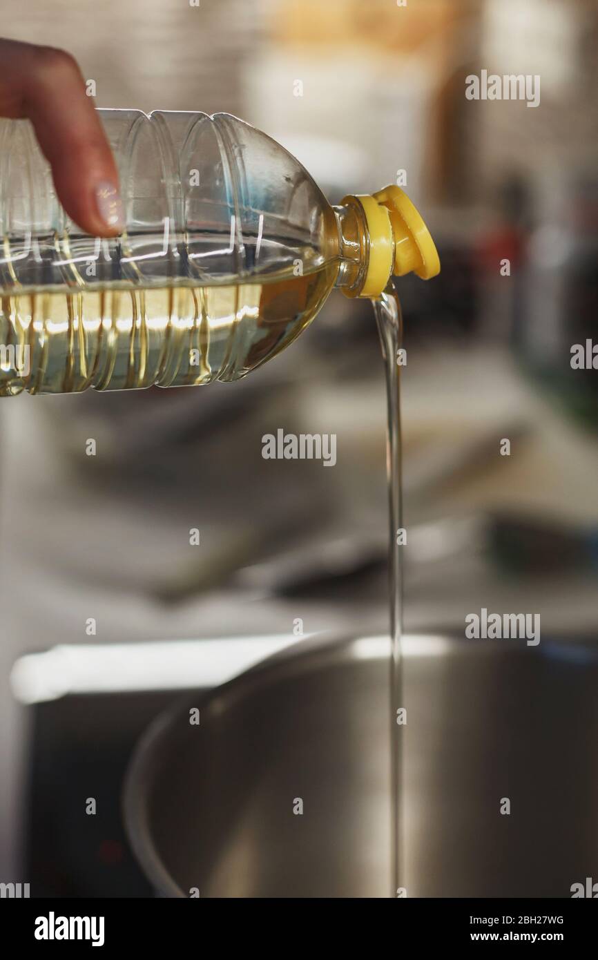 Close up of pouring vegetable oil into deep cooking stainless steel pot ...