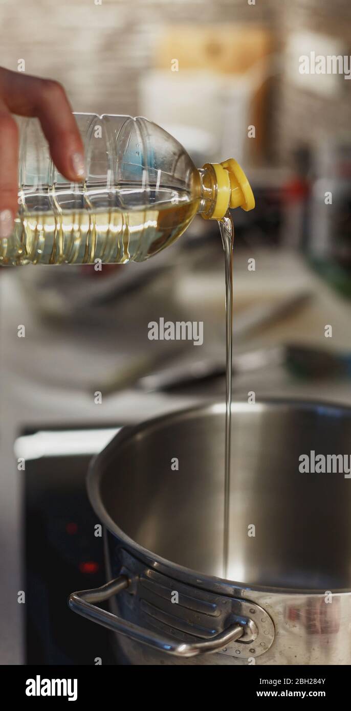 Close up of pouring vegetable oil into deep cooking stainless steel pot ...