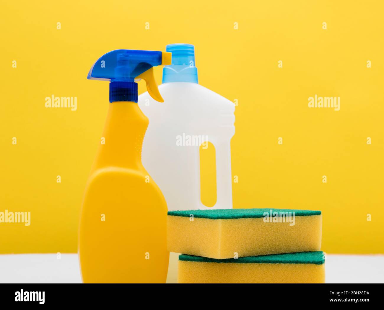 Cleaning spray bottles and cloths against a bright yellow background ...