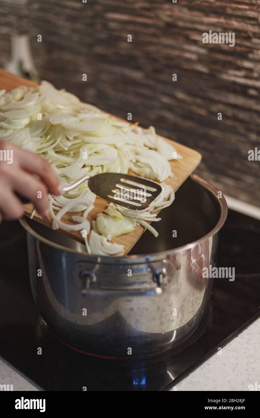 Process of placing fresh sliced onions into stainless steel cooking pot ...