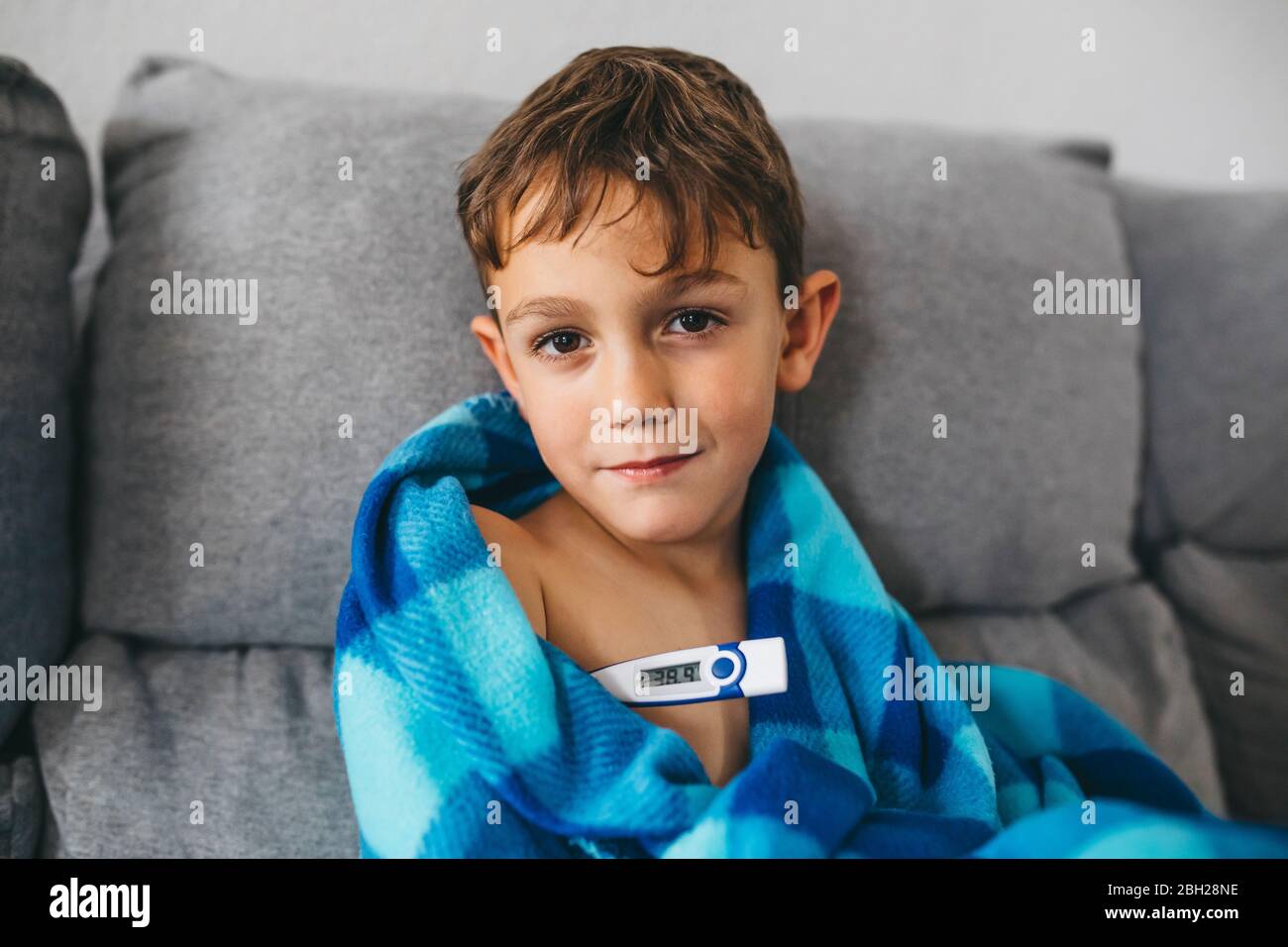 Portrait of sick boy sitting on couch with digital thermometer Stock ...