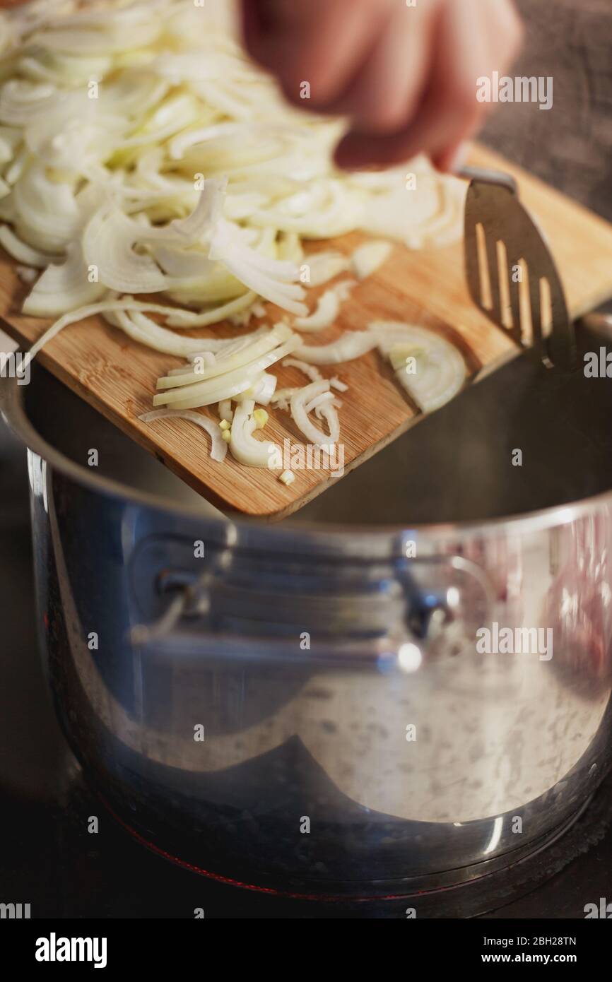 Process of placing fresh sliced onions into stainless steel cooking pot ...