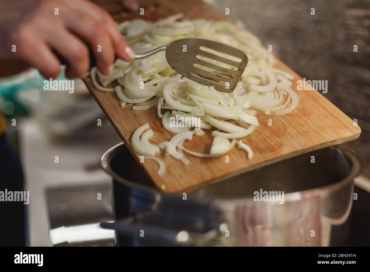 Process of placing fresh sliced onions into stainless steel cooking pot ...