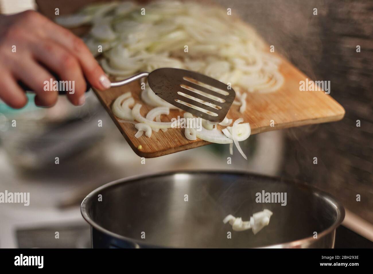 Process of placing fresh sliced onions into stainless steel cooking pot ...
