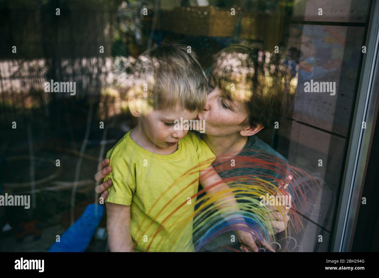 Mother kissing her little son behind window with drawn rainbow Stock ...