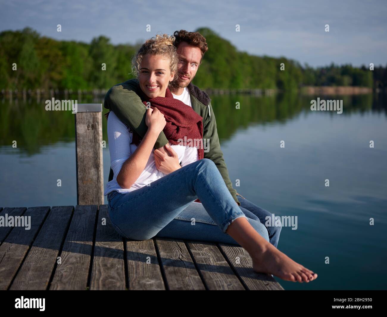 Romantic couple sitting on jetty at the lake Stock Photo - Alamy