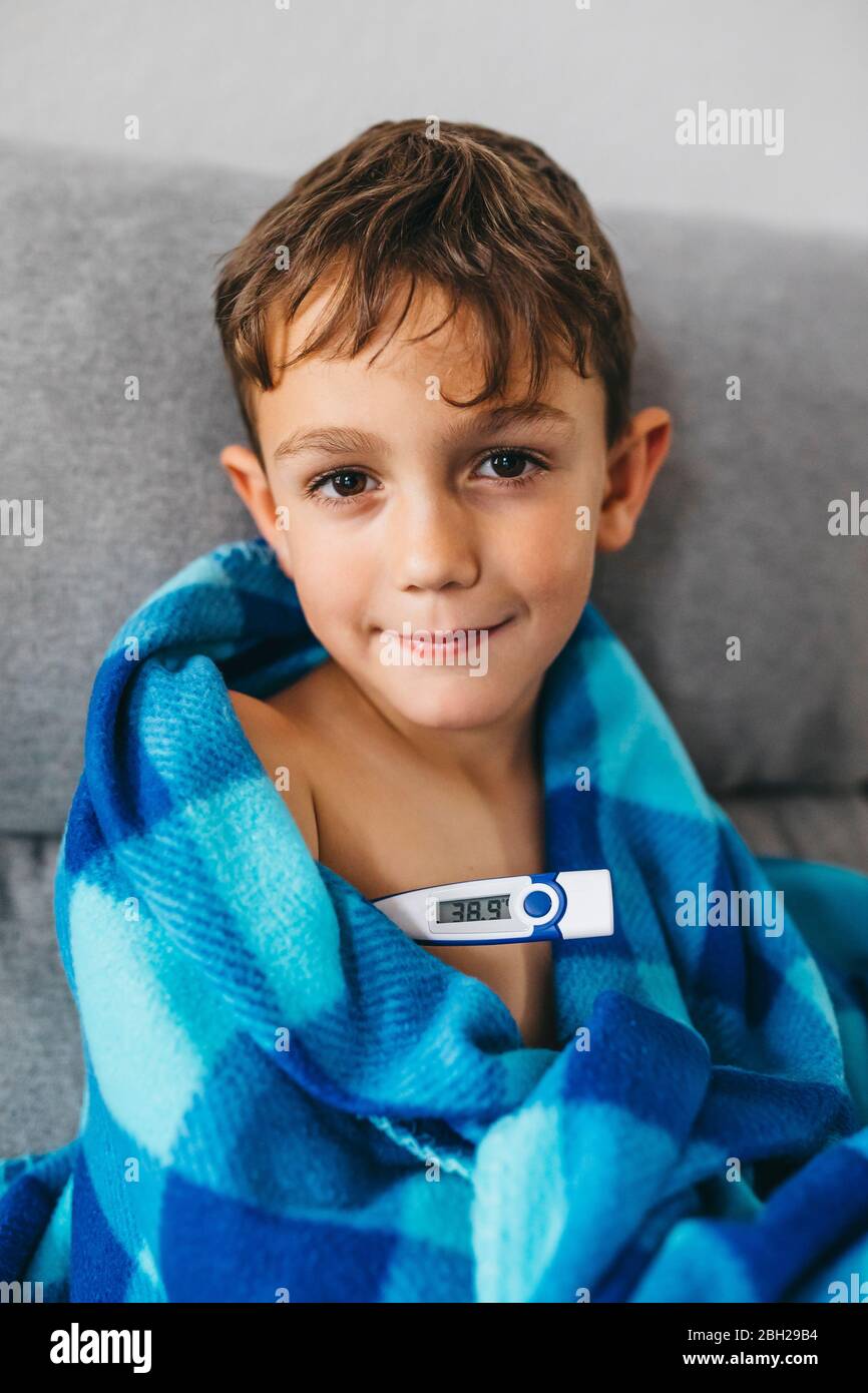 Portrait of sick boy sitting on couch with digital thermometer Stock ...