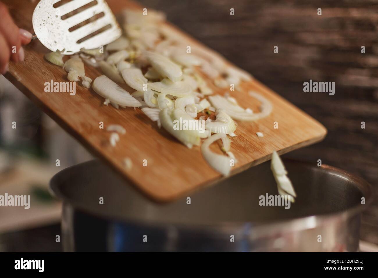 Process of placing fresh sliced onions into stainless steel cooking pot ...