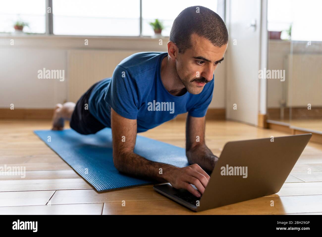 Man doing a plank and using laptop at home Stock Photo - Alamy