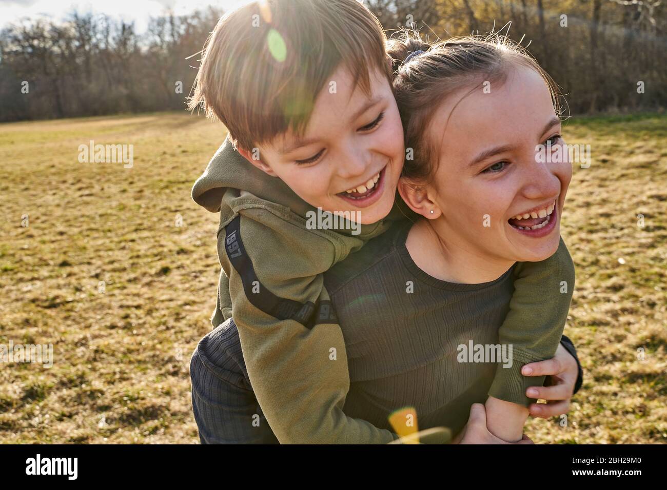 Happy girl carrying brother piggyback on a meadow Stock Photo - Alamy