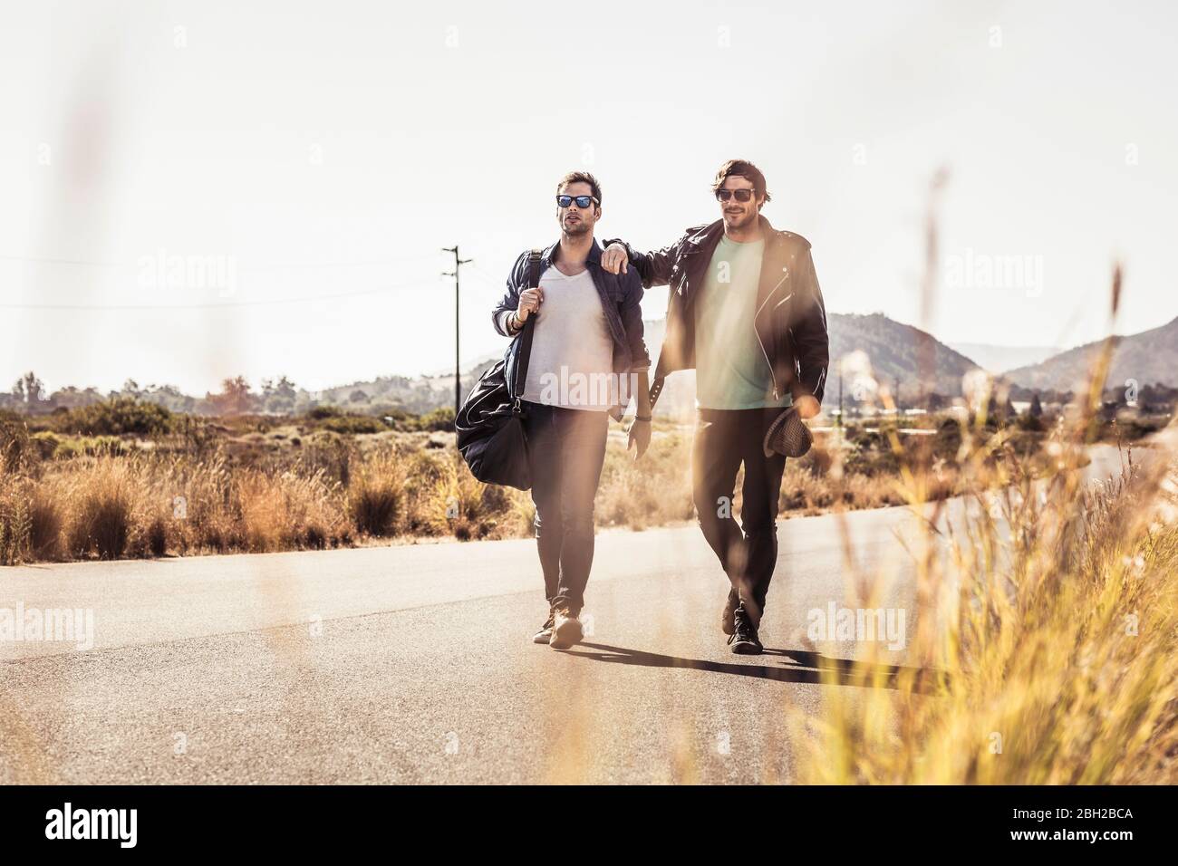 Two men with travelling bag walking on country road Stock Photo - Alamy