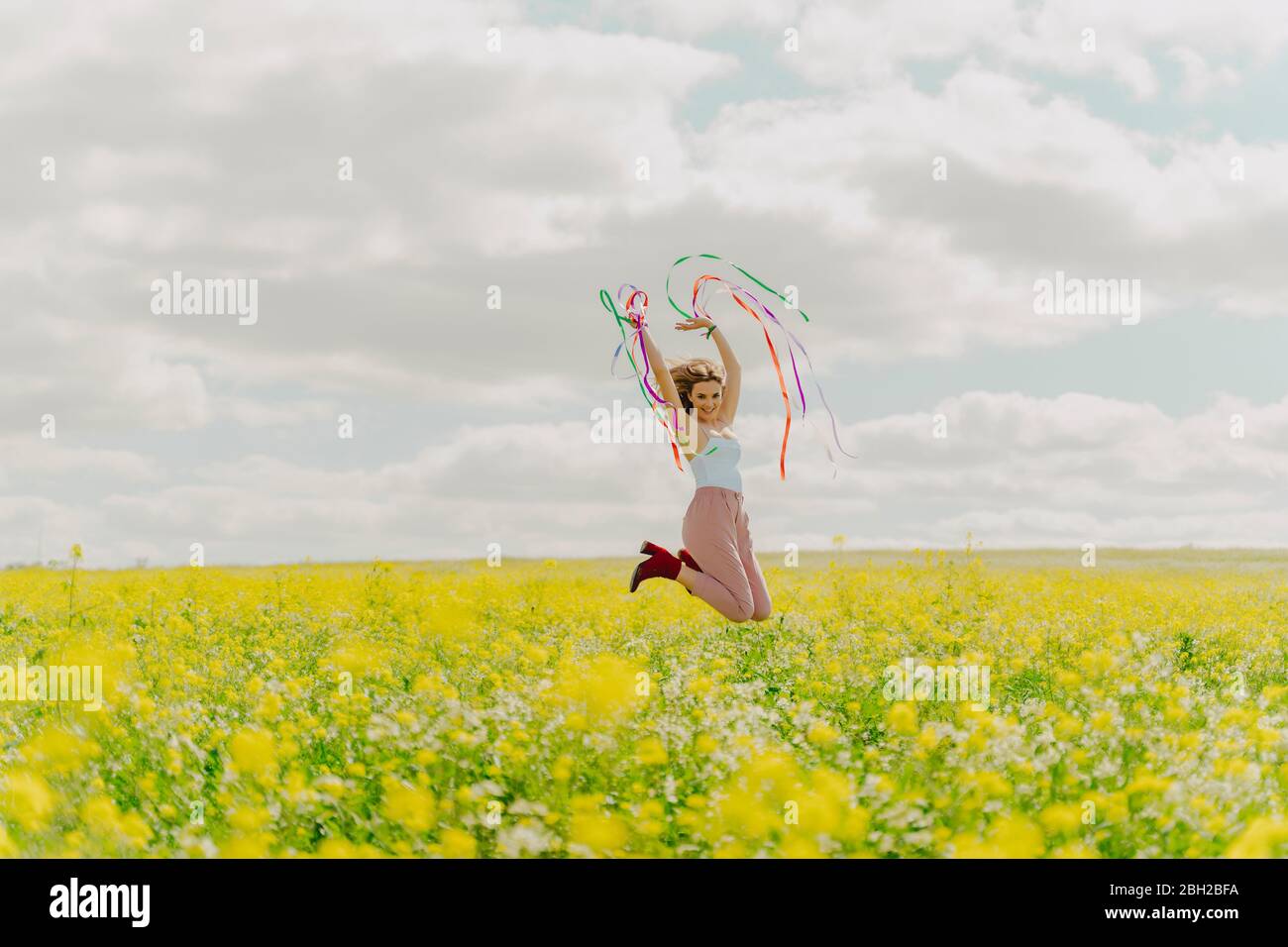 Happy young woman jumping with colourful ribbons in a flower meadow in ...
