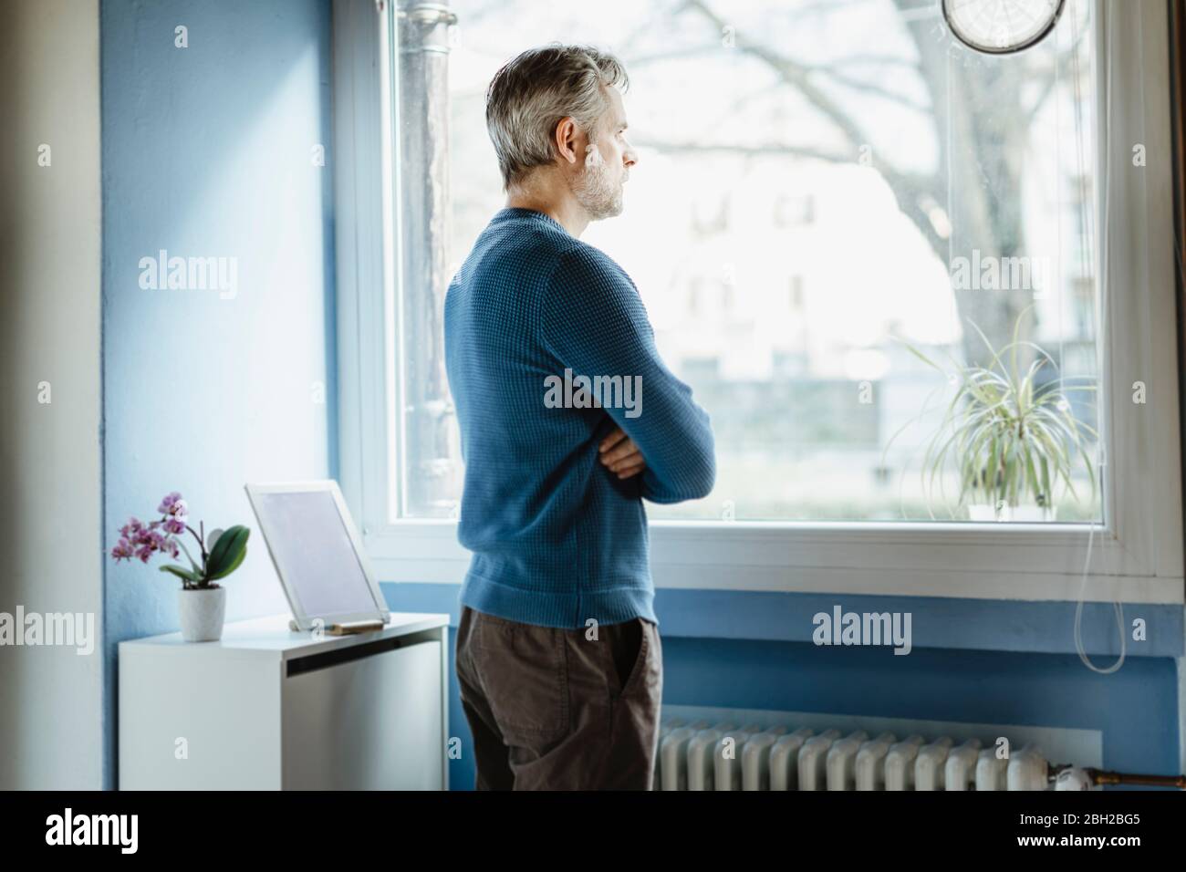 Pensive man standing in living room looking out of window Stock Photo ...