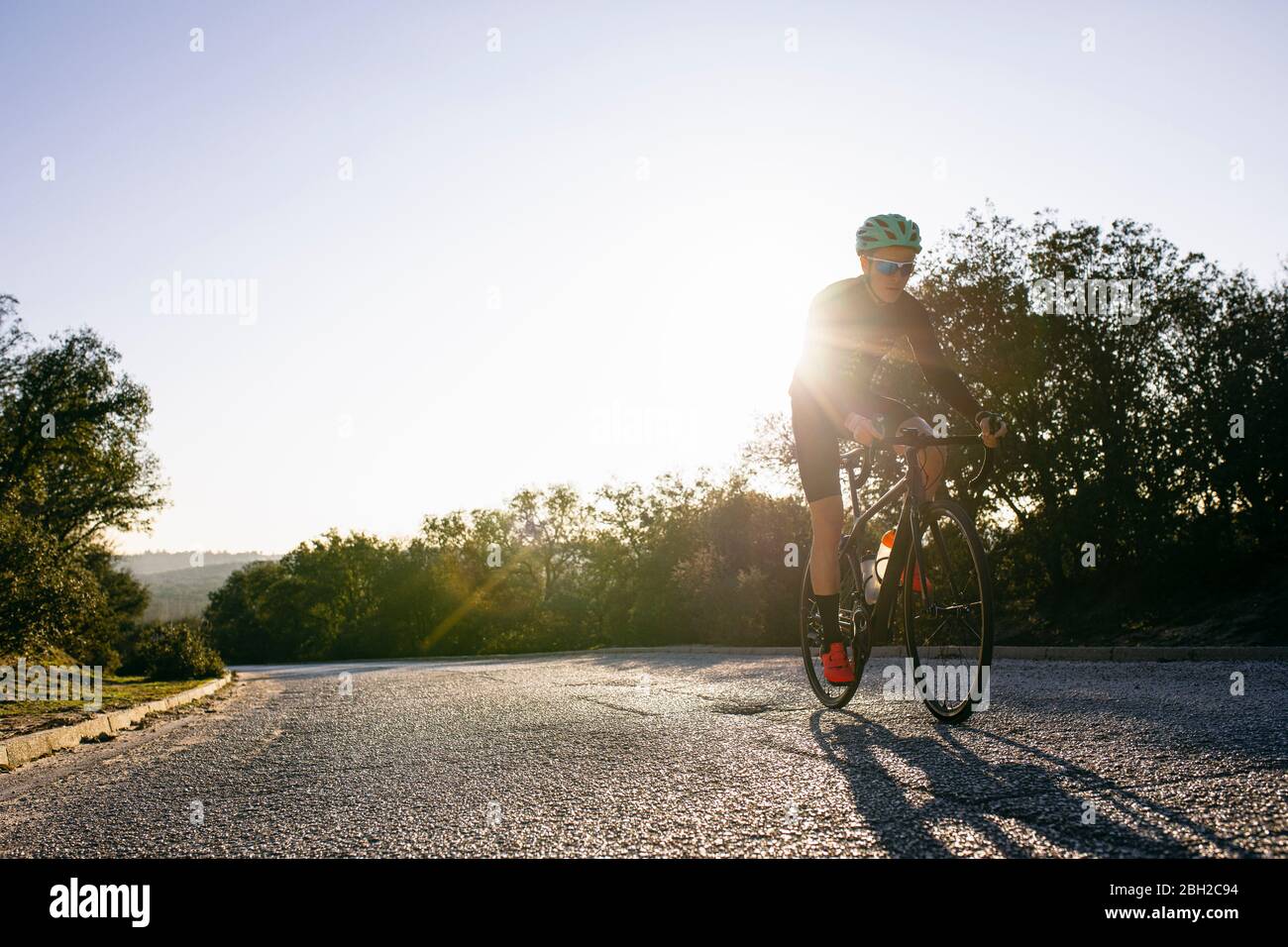 Athlete riding bicycle on country road at sunset Stock Photo - Alamy