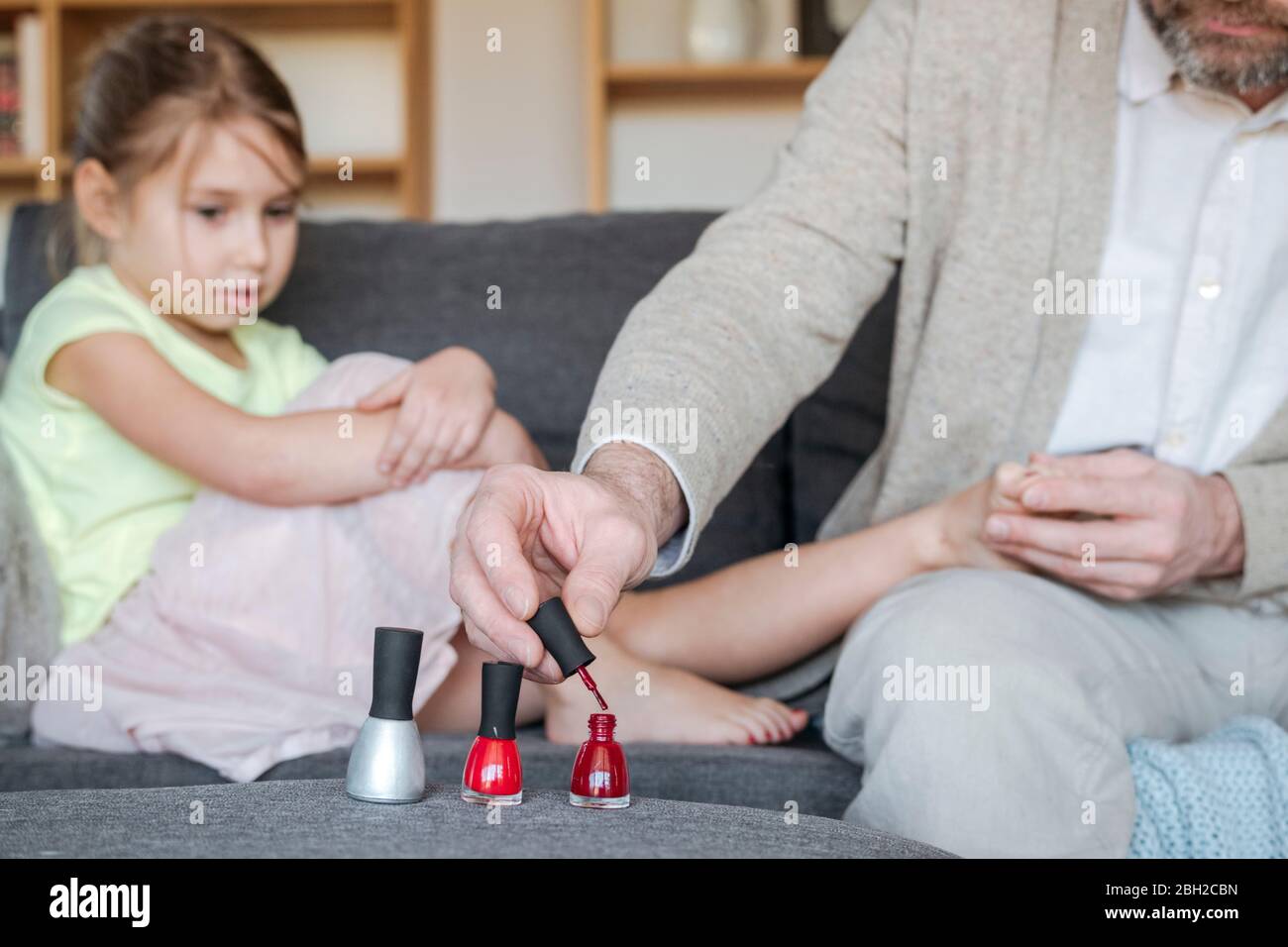 Crop view of father painting his daughter's toenails with red nail ...