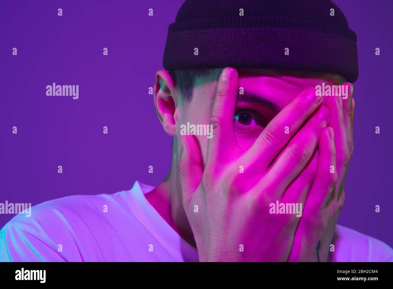 Scared hiding face. Caucasian man's portrait isolated on purple studio ...