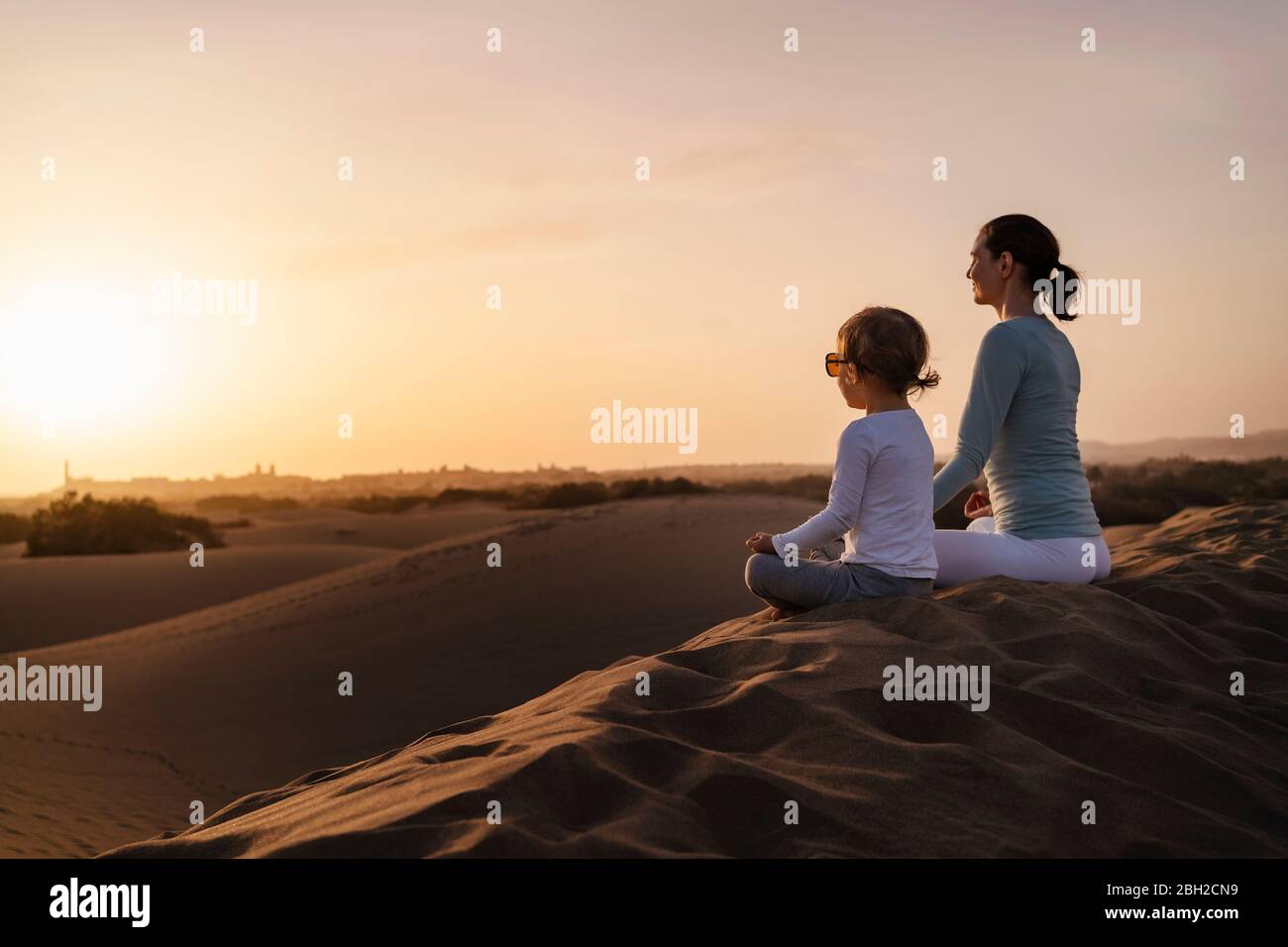Mother and daughter practicing yoga in sand dunes at sunset, Gran ...