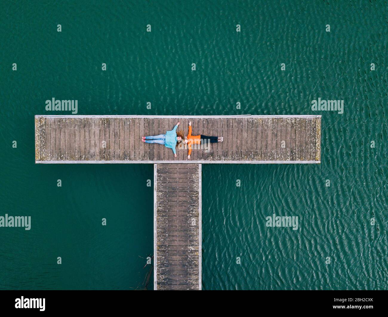 Two women lying on jetty with arms outstretched, Valdemurio Reservoir ...
