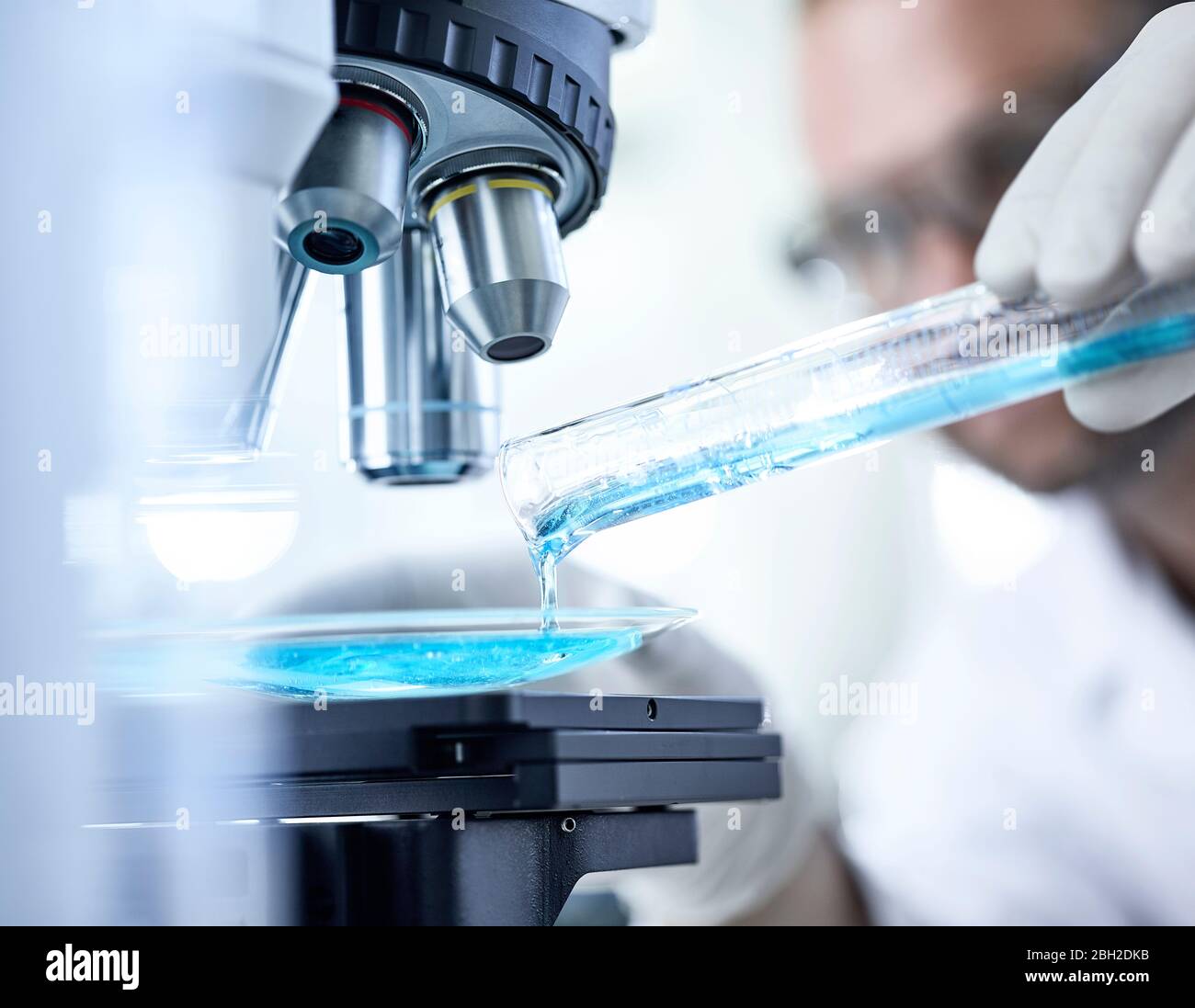 Scientist pouring blue liquid in bowl under microscope Stock Photo - Alamy