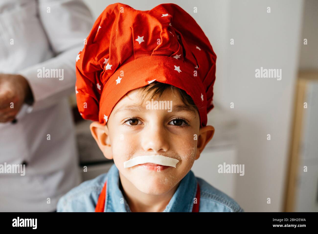 Portrait of playful boy with pasta fake moustache in kitchen at home ...