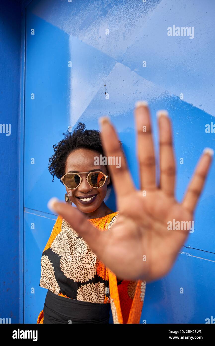 Portrait of smiling woman raising her hand in front of blue background ...
