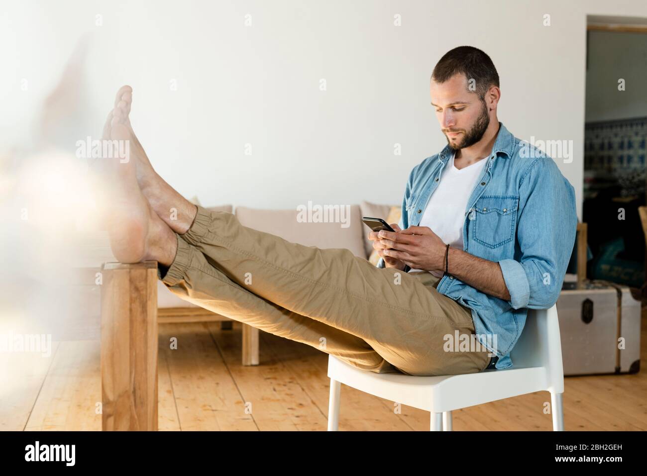 Young man at home typing on his smartphone in modern living room with ...