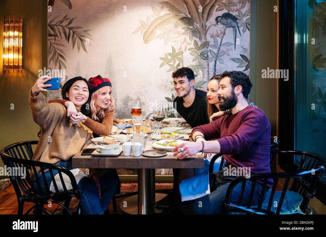 Friends having dinner in a fancy restaurant, taking smartphone selfies ...