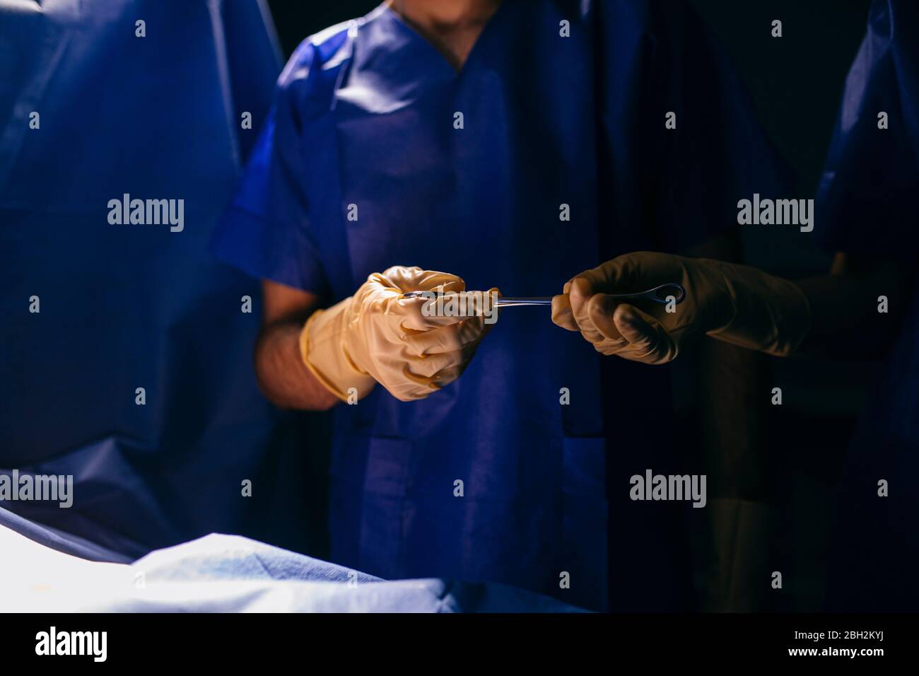 Operating room nurse passing surgical instrument to surgeon during ...