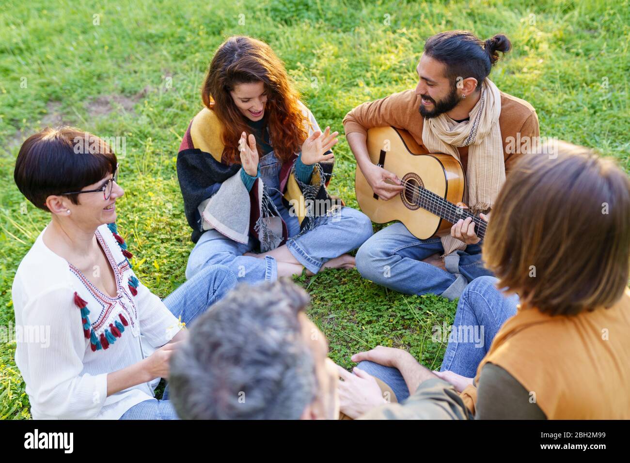 Group of friends playing music with the guitar sitting on the grass in ...