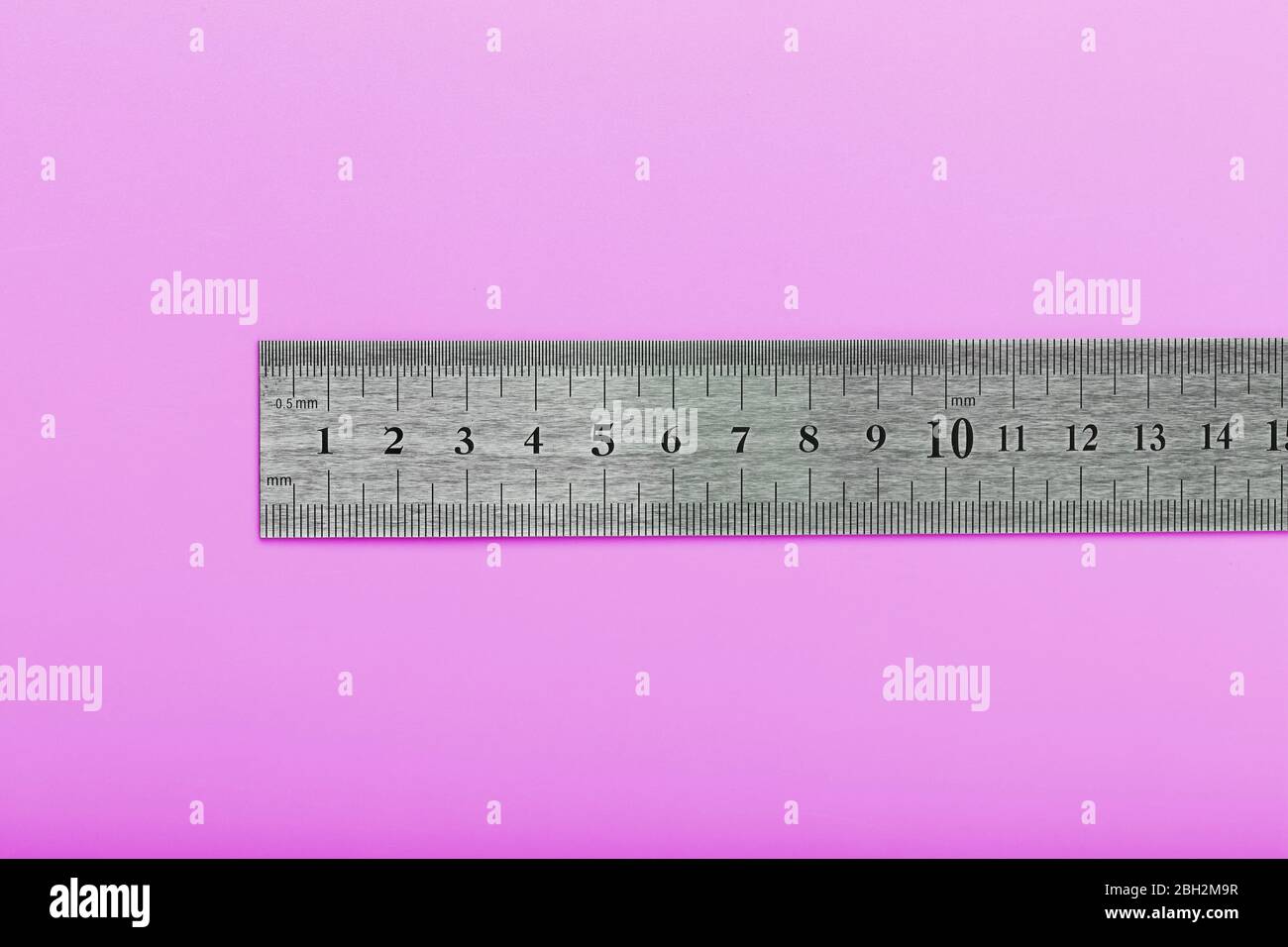 A metal ruler with a scale on a pink background is a superscape with a ...