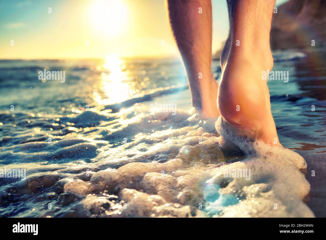Closeup of a man's bare feet walking at a beach at sunset touching the ...