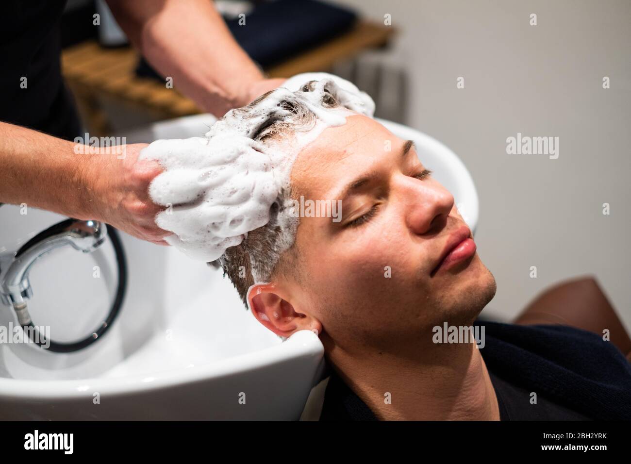 Barber washes young man's hair with lots of foam in his barbershop ...