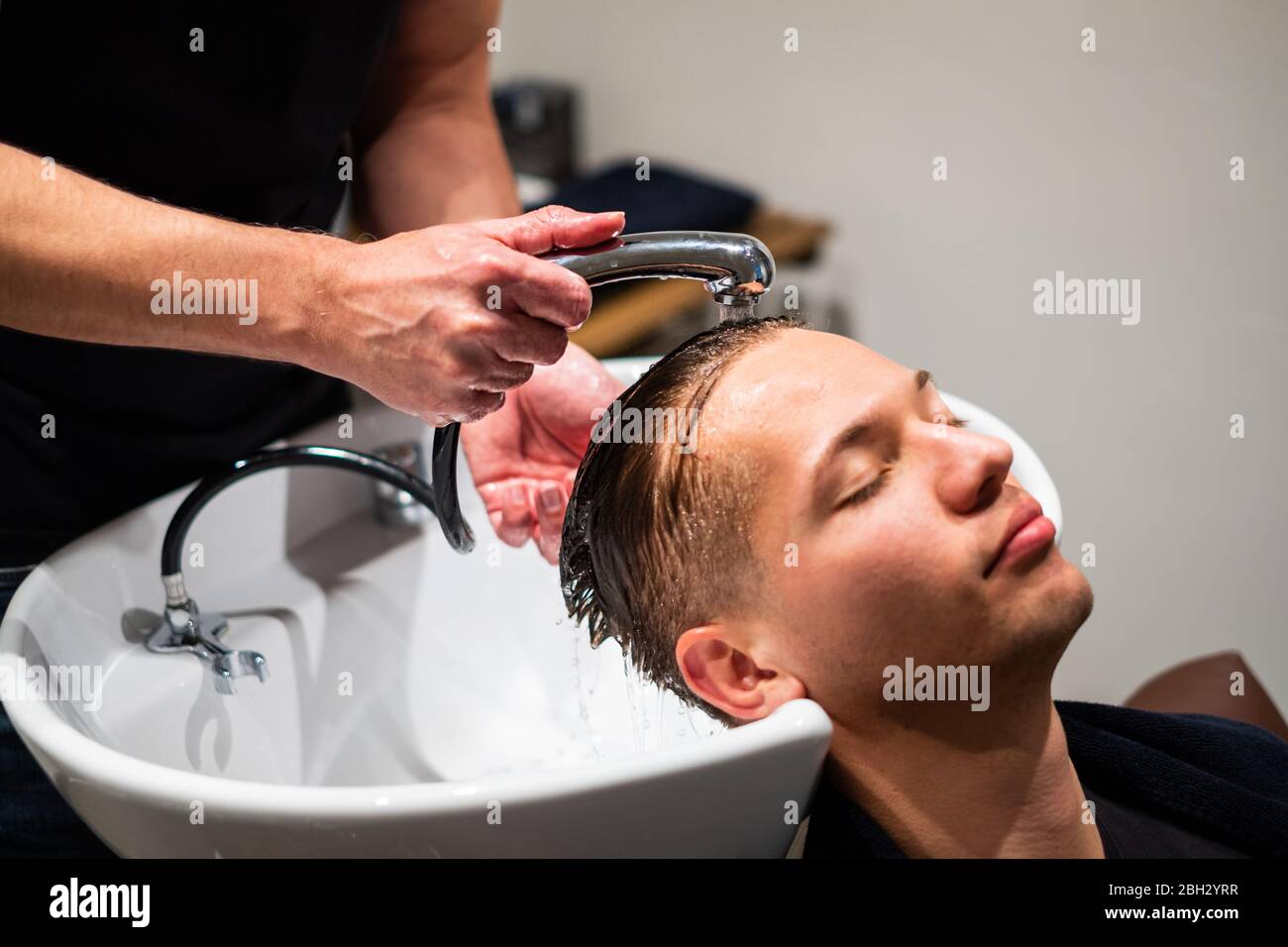 Barber washes with water from the tap young man's hair over the sink in ...