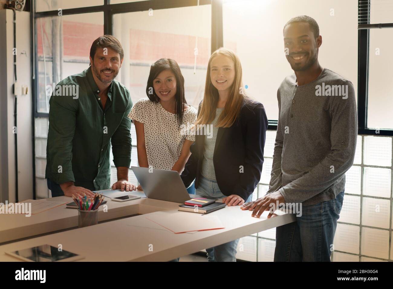 Four attractive co workers standing in modern office smiling at camera ...