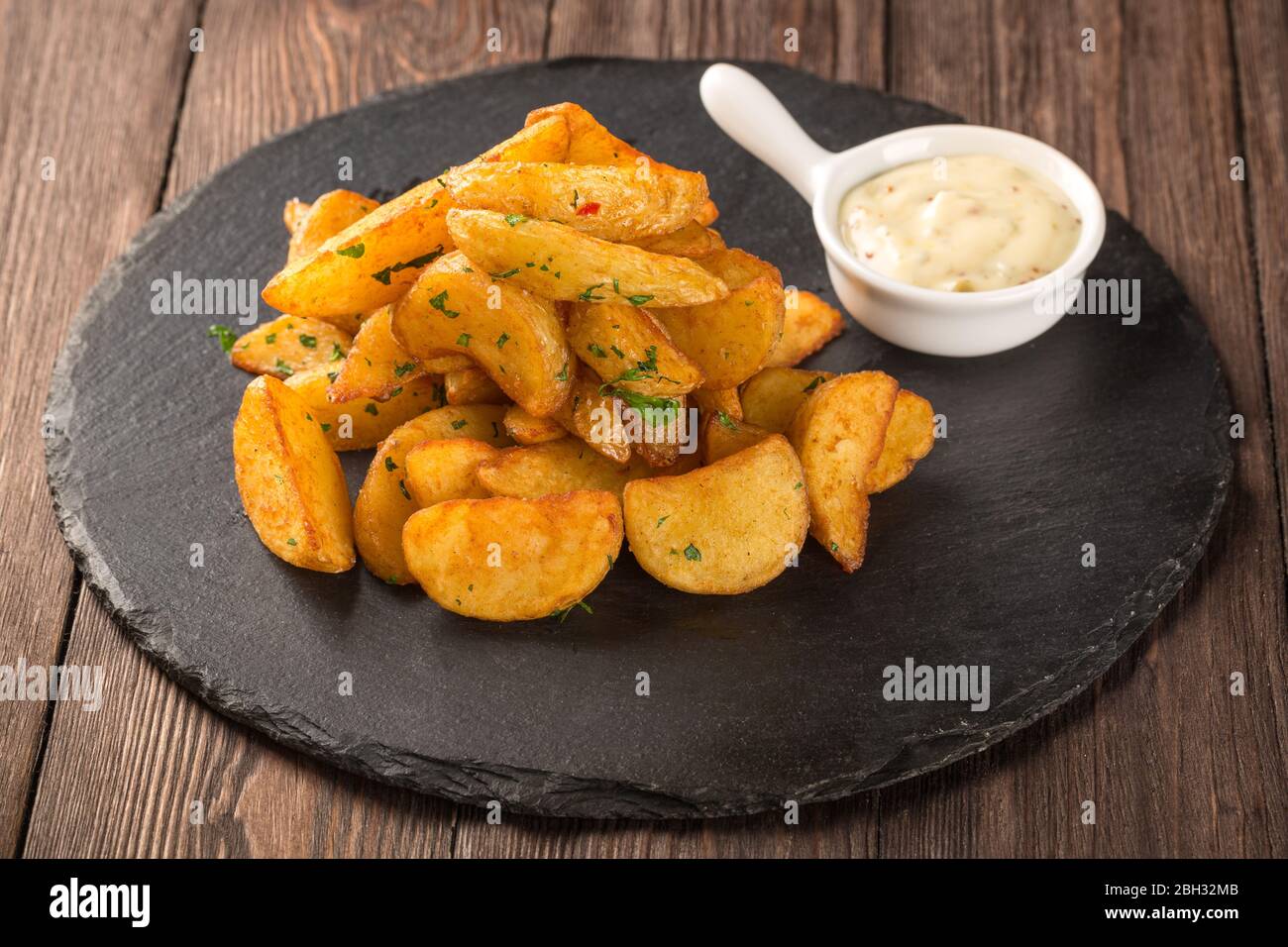 Fried potato wedges on a round black board with mustard sauce Stock ...