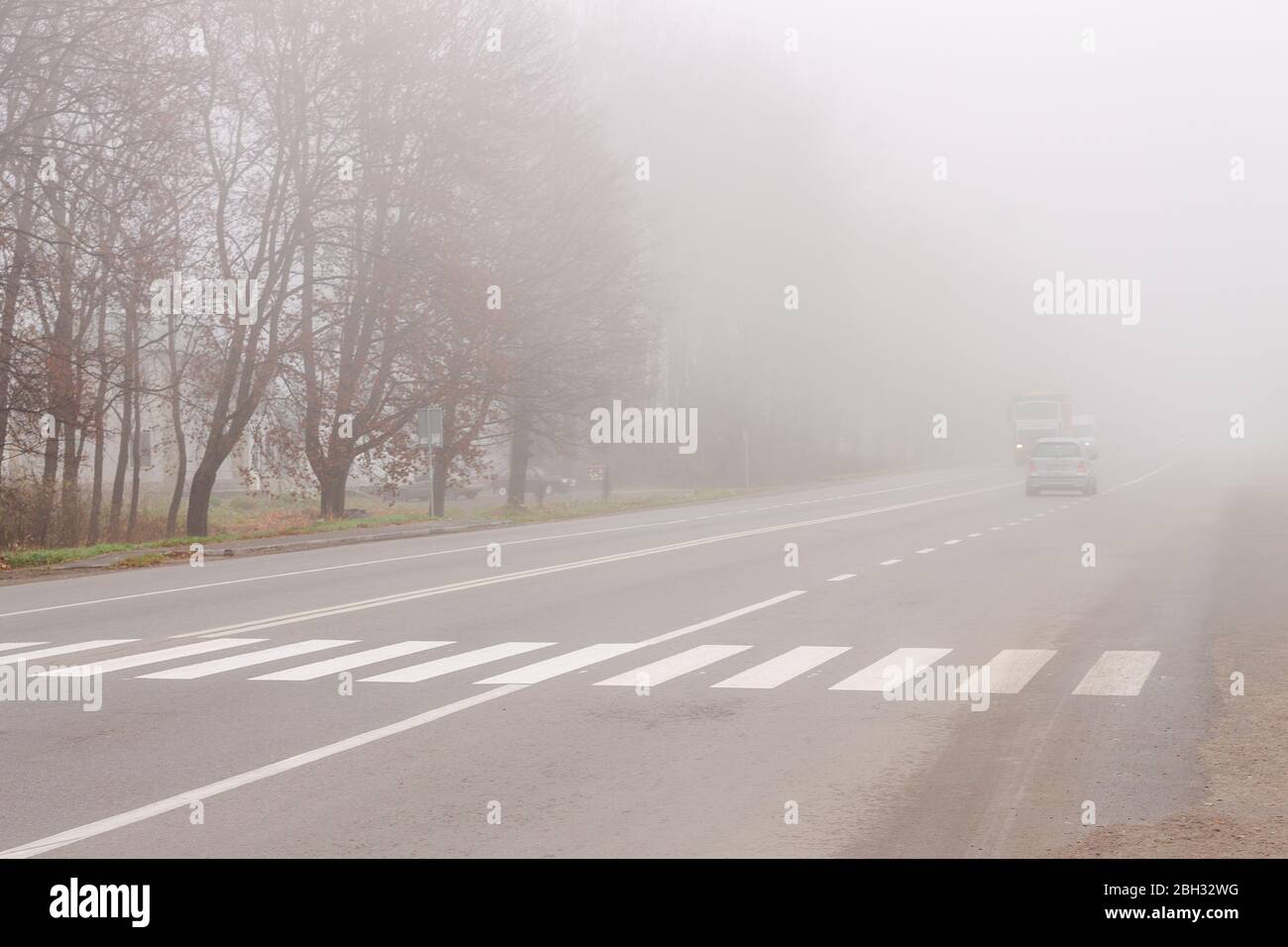 Thick misty fog and crosswalk in road with traffic, danger on the way ...