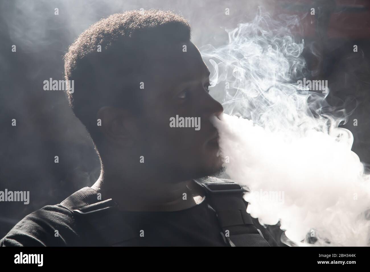 Portrait of a black boy smoking from a vapper and blowing the smoke ...