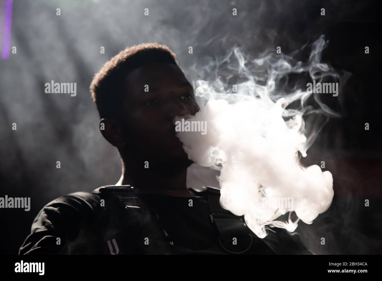 Portrait of a black boy smoking from a vapper while is sitting in a ...