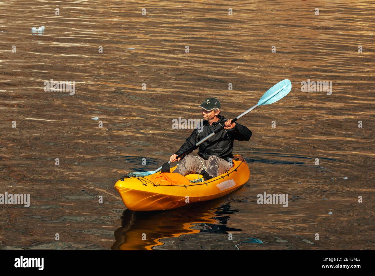 A male rowing in a yellow kayak on a sea in Greenland during summer ...