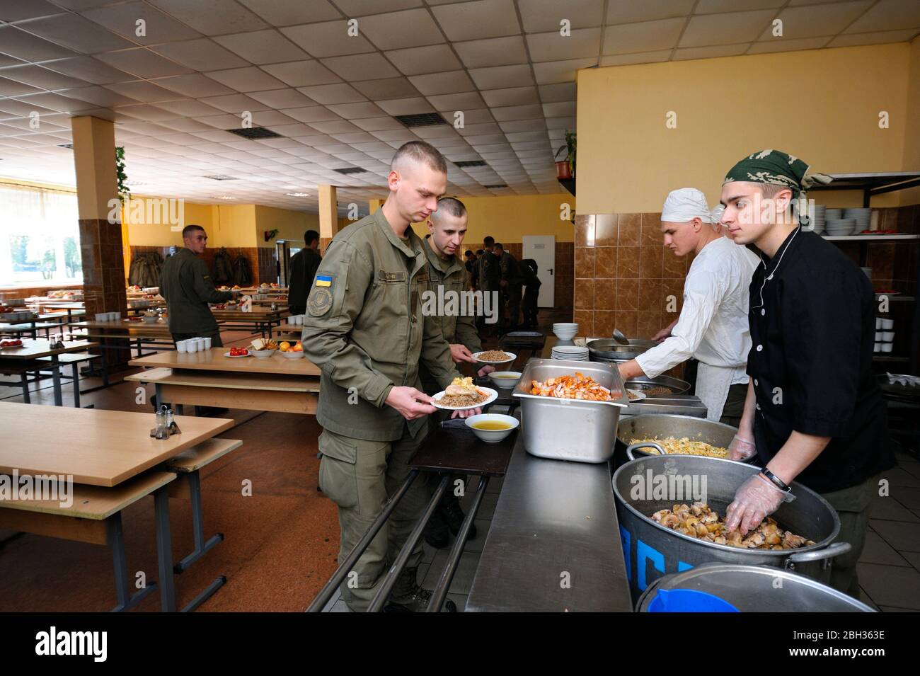At a chow hall: soldiers stand in front of a serving bar and wait for ...