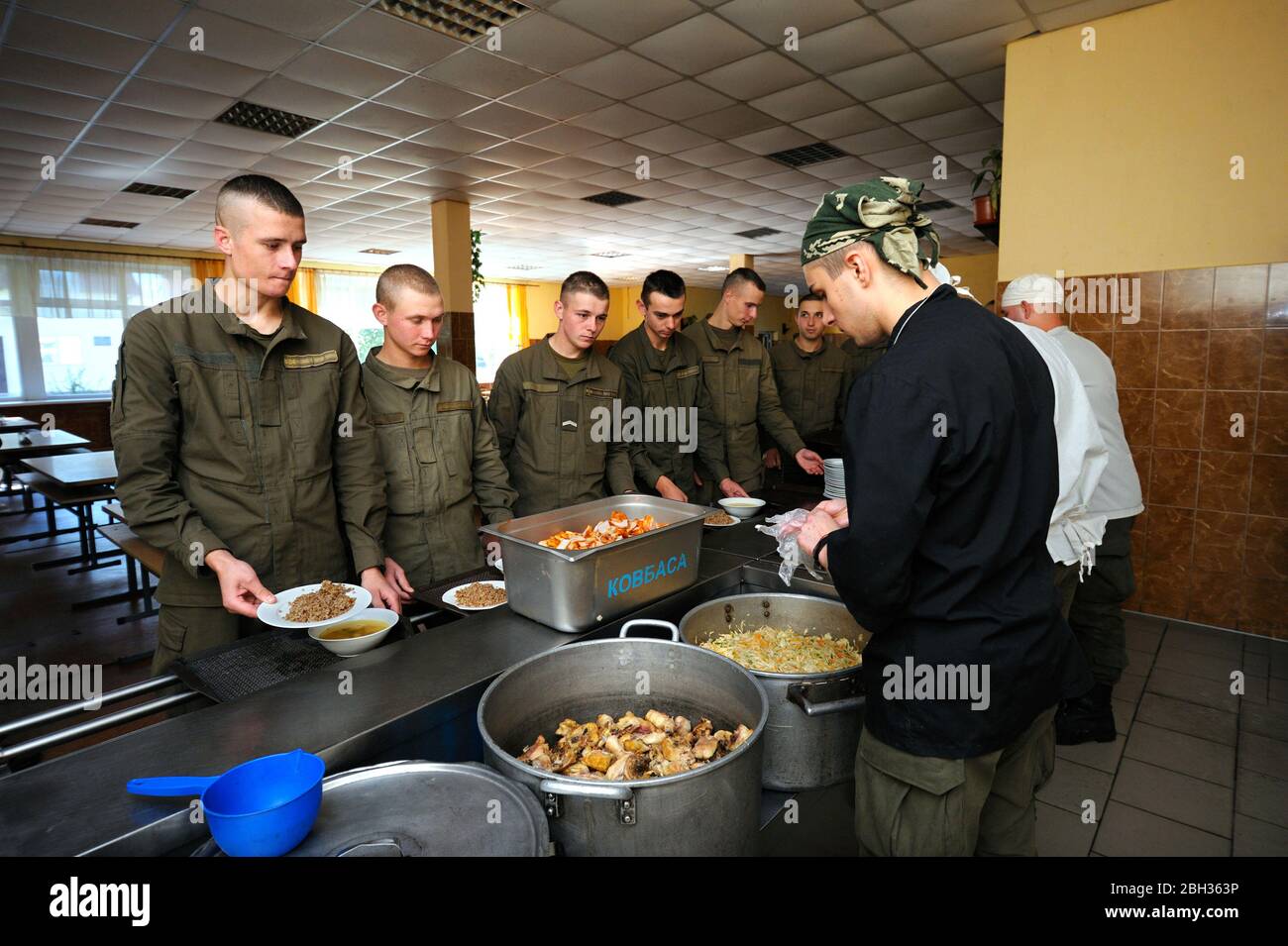 At a chow hall: soldiers stand in front of a serving bar and wait for ...