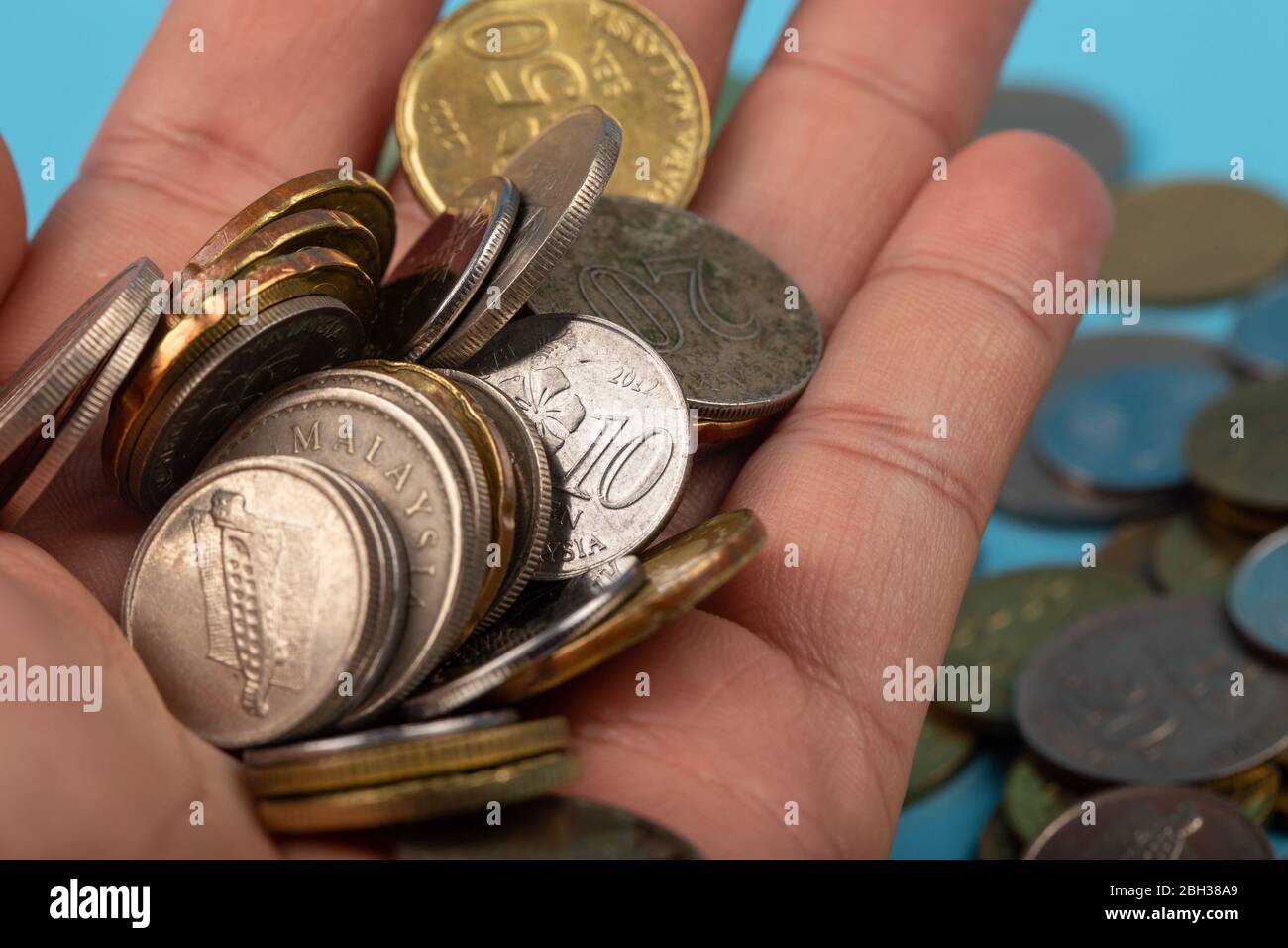 Man hand holding coin on blue background Stock Photo - Alamy