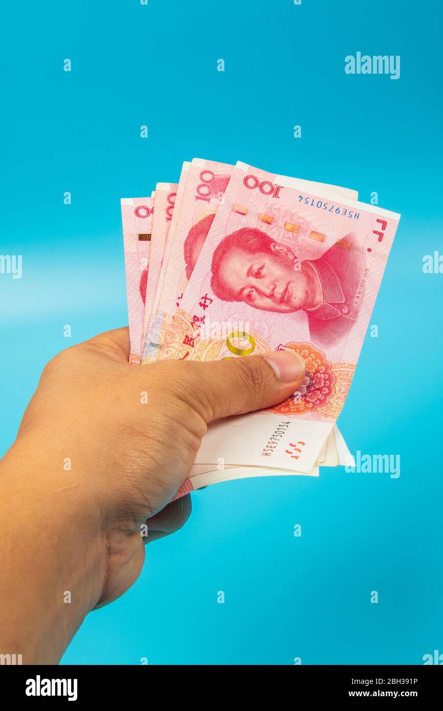 Man hand holding China Note RMB100 Yuan Note on blue background Stock ...