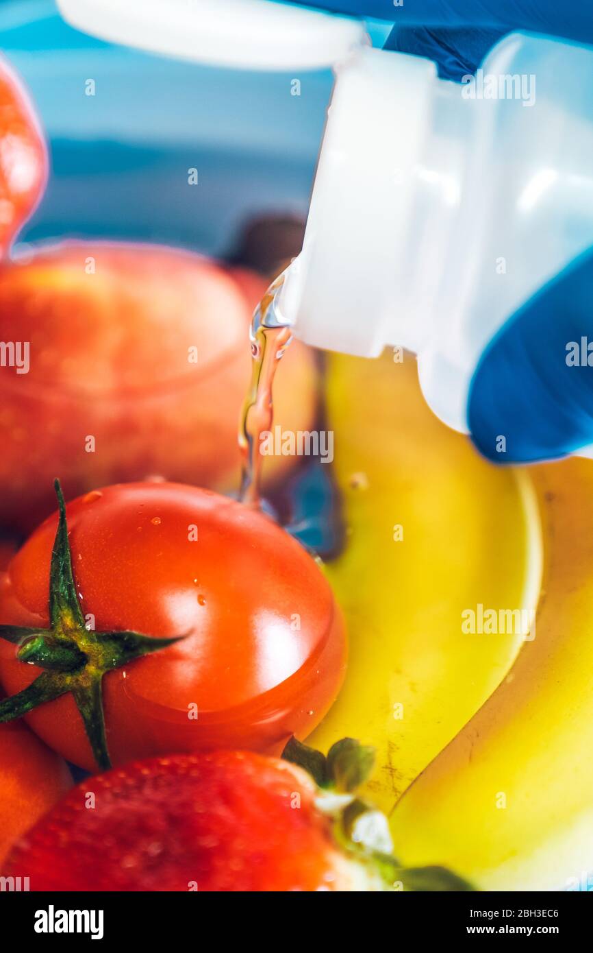 Hand pouring bleach into a plastic bowl with different fruits and water ...